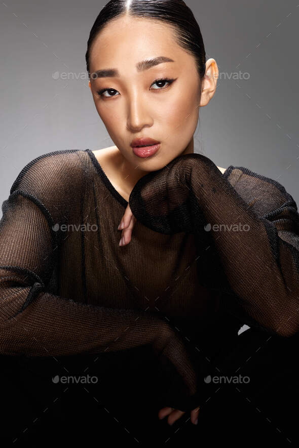 Fashion asian woman in sheer top sitting on chair with hands on hips ...