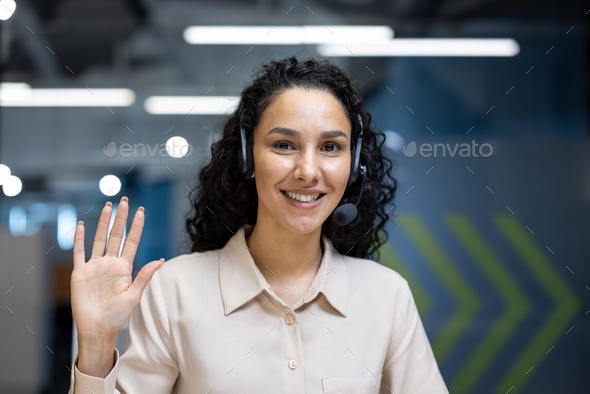 Smiling call center representative wearing headset waving hand in ...