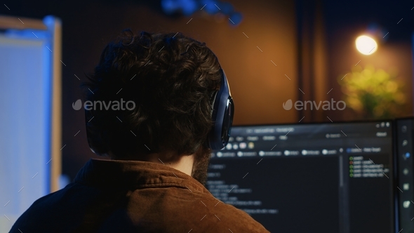 Technician listening music while using coding to fortify firewalls Stock Photo by DC_Studio