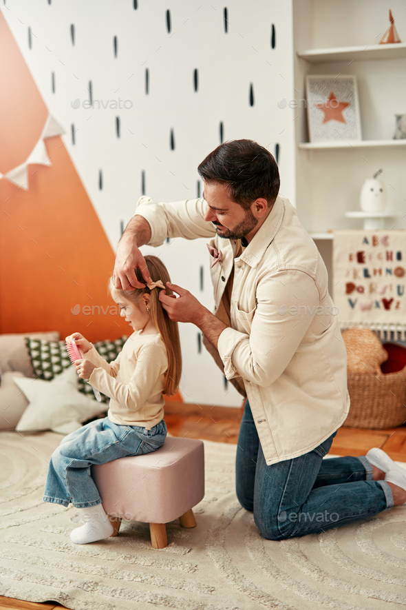 Father braids daughters hair in a warm, snug room, cherishing a moment ...