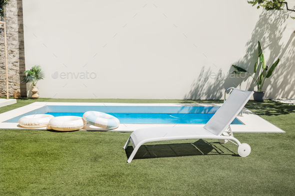 A pool deck view on a bright sunny day. The pool area has white walls ...