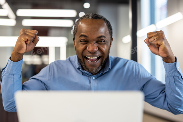 Happy african american office worker celebrating success at workplace ...