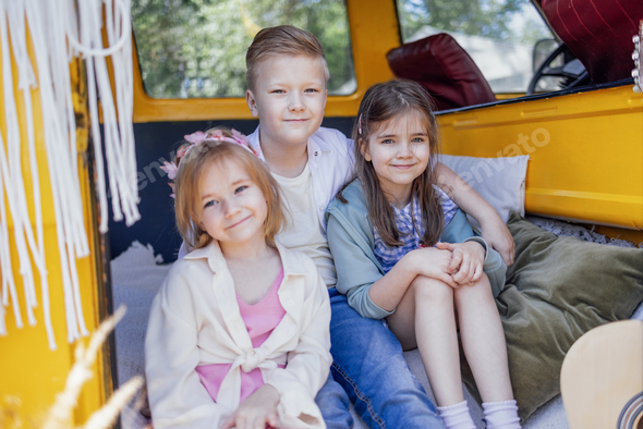 Three cute little kids are sitting inside retro minivan in boho style ...