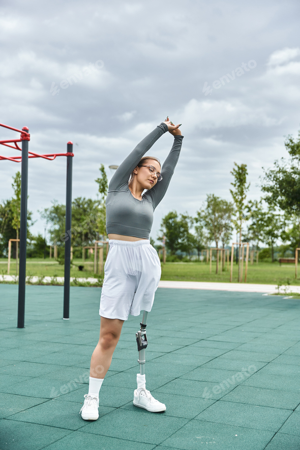 Empowered young woman with prosthetic leg stretching in park while ...