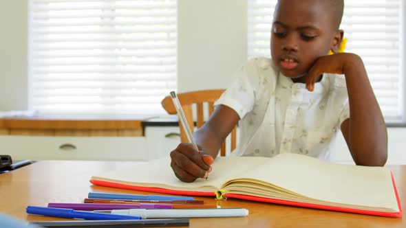 Front view of little black boy doing homework at dining table in a ...