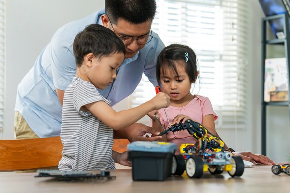 A boy and girl are learning to build robot toys with their dad in the ...