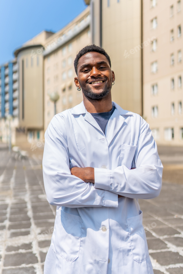 Smiling african doctor standing with arms crossed outside the hospital ...