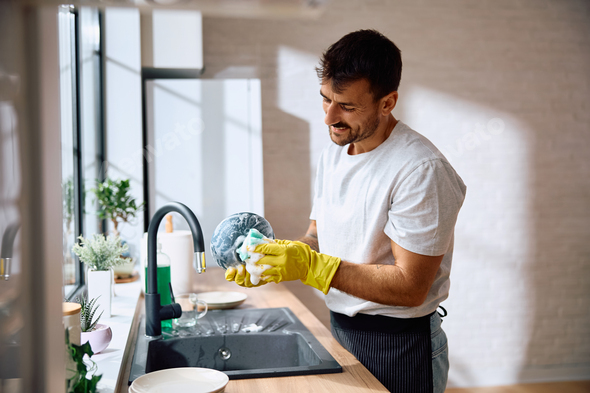 Smiling man washing dishes in the kitchen. Stock Photo by drazenphoto