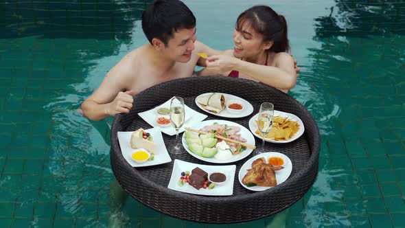 happy young couple enjoying and eating floating food in swimming pool ...