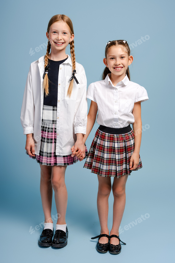 Two smiling schoolgirls holding hands wearing school uniform Stock Photo by msvyatkovska