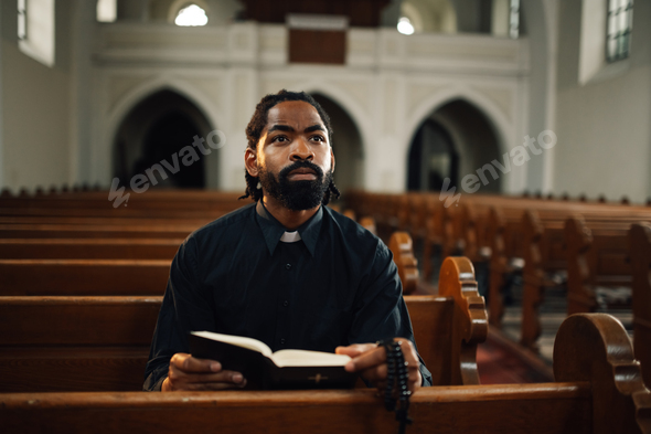 Priest praying with rosary beads and open bible in church pews Stock ...