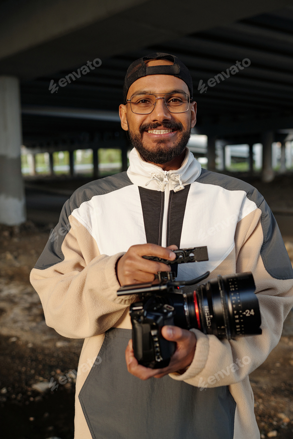 Smiling Man Holding Camera Underneath Concrete Structure Stock Photo by ...