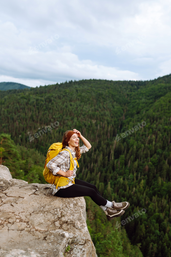 Beautiful traveler with a yellow hiking backpack observes the mountain ...