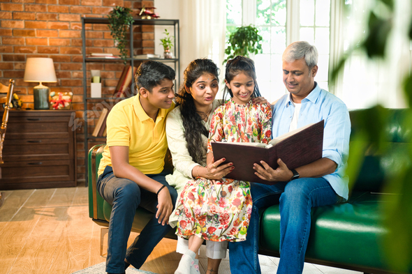 Indian family of four happily reminiscing while looking through a photo ...