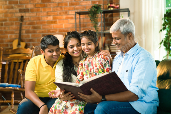 Indian family of four happily reminiscing while looking through a photo ...