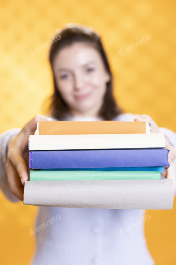 Portrait of joyous reading enthusiast offering books, studio background ...