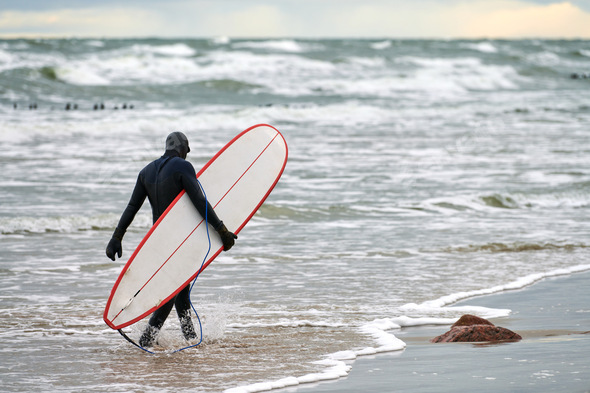 Male surfer in swim suit walking along sea with surfboard Stock Photo ...