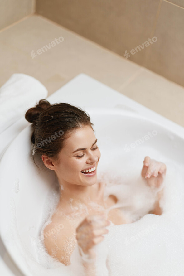 Joyful young woman enjoying a relaxing bubble bath, smiling with ...