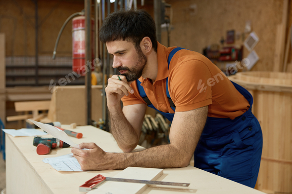 Pensive man carpenter reading blueprints and thinking during ...