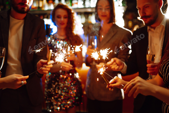 Glowing sparkles in hands. Group of happy people enjoying party with ...