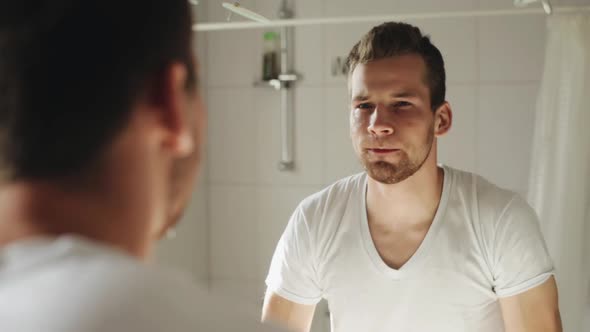 A Handsome Young Man Washing His Face. Looks in the Mirror. Serious ...