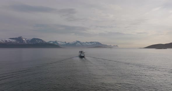 Ferry sailing towards snowy mountains on Senja Island, Norway; aerial ...