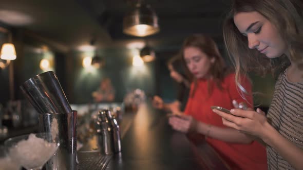 Three Busy Young Girls Sit By the Bar Waiting for Cocktails and Typing ...
