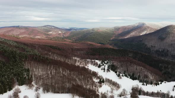 Wide angle flyover above forested foothills with a light dusting of ...