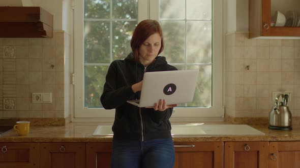 30s Woman Working From Home Using Laptop Standing in the Kitchen By the ...
