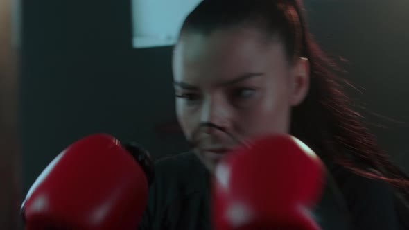 Slow motion sportive woman boxer in boxing gloves trains in a dark gym ...