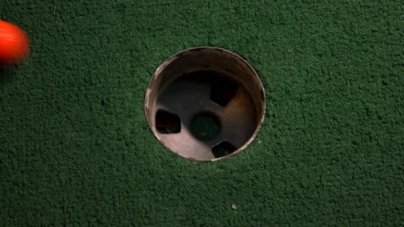 A close up birds eye view of an orange mini golf ball falls into the ...