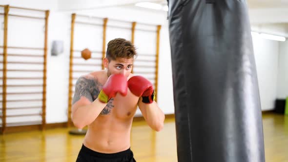 Young guy trains in a gym and fists his boxing bag fist, Stock Footage
