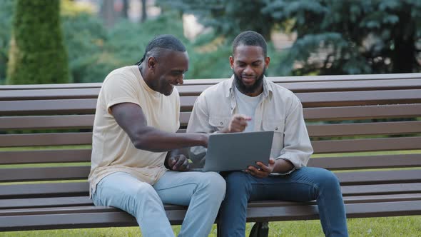 African American Black Male Friends Sitting in Park Looking at Computer ...