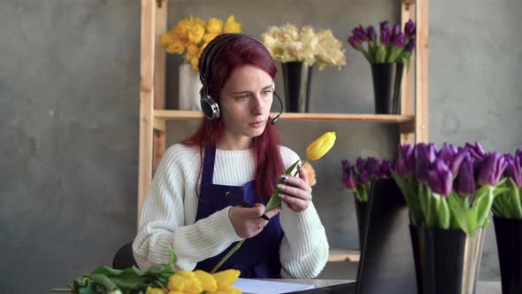 Florist in Headphones with a Microphone and an Apron Sits at a Table in ...