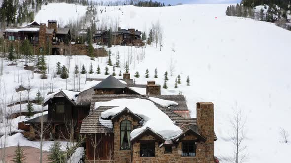 Modern slopeside winter homes during snowfall, aerial drone fly over ...