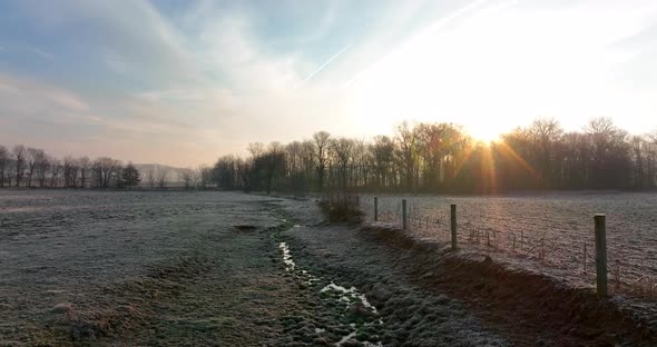 Stream through meadow pasture in winter frost at sunrise. Water ...