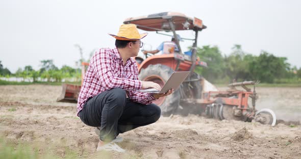 Man squatting in corn field using laptop with tractor, Stock Footage