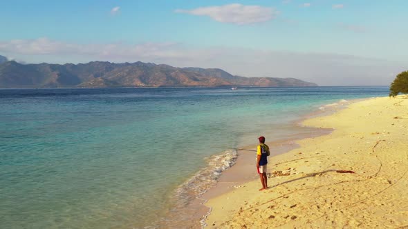 Male model fishing on marine lagoon beach break by aqua blue ocean with ...