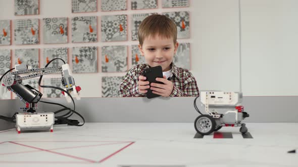 Little Boy Controls a Robot Using His Phone in a Robotics Class, Stock ...