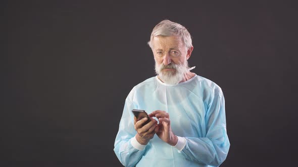 Portrait of Old Surgeon. Old Surgeon Uses Smartphone on Dark Background ...