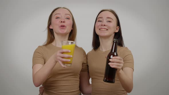 Twins Toasting Healthful Juice and Beer Bottle Smiling Looking at ...