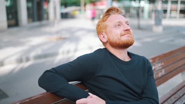 Positive ginger man texting by smartphone and breathing while sitting ...