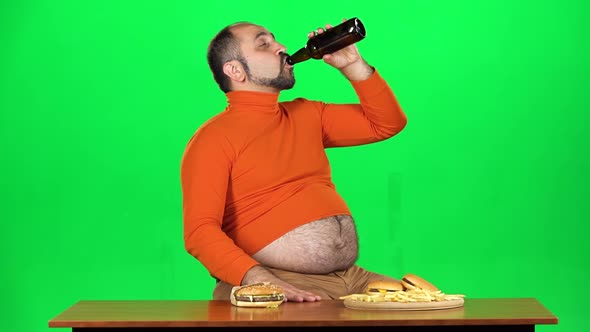 Overweight Caucasian Man Sits at a Table with Junk Food, Drinks Beer ...