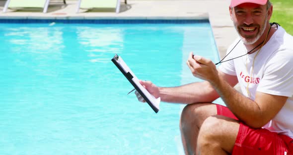 Lifeguard sitting at pool side holding clipboard and stop watch, Stock ...