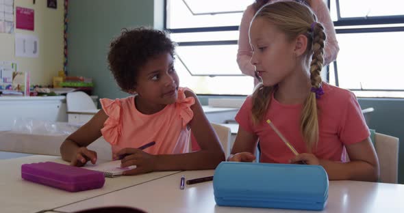 Two girls talking to each other while studying in the class by ...