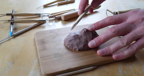 Close up on the hands of an artist sculpting with brown modeling clay ...