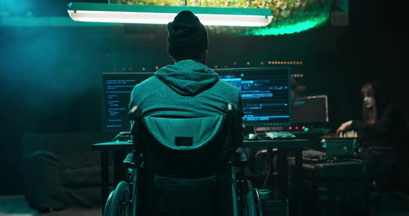 Shot From the Back to Man in a Wheelchair a Hooded Hacker Works on a ...