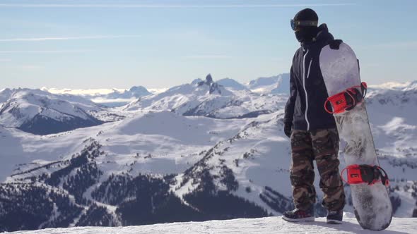 A young man snowboarder standing with his snowboard on a snow covered ...