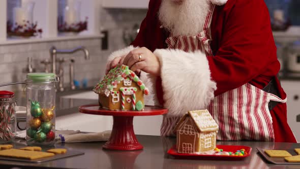 Santa Claus in kitchen decorating gingerbread house, Stock Footage