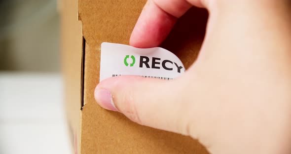 Hands applying RECYCLE Sticker label on a cardboard box with barcode ...